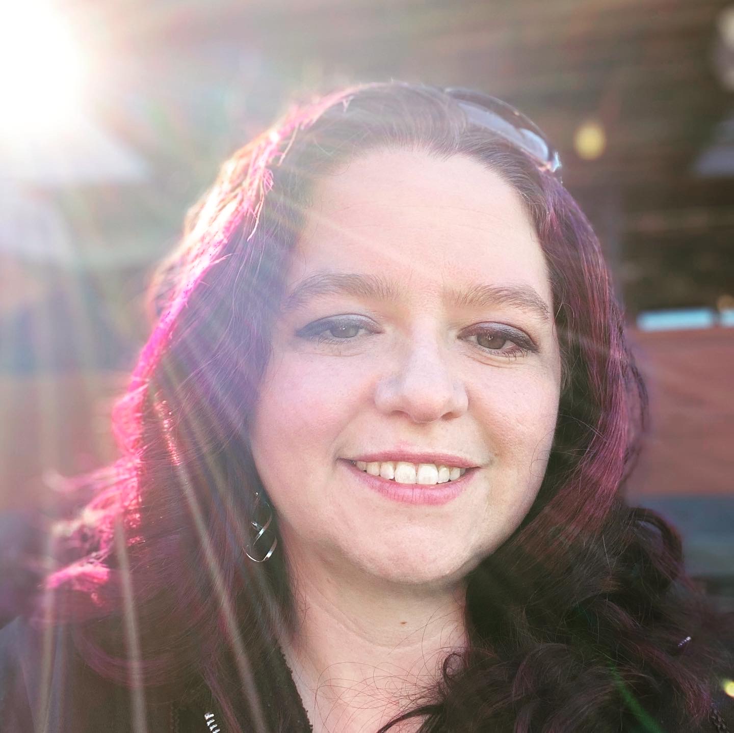 Smiling woman with long dark hair against a sunbeam