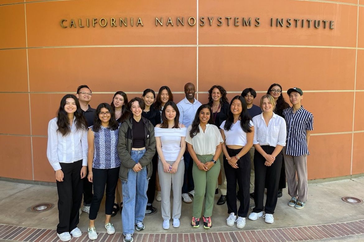 Photo | Group of 16 people stand in two rows in front of wall reading ...
