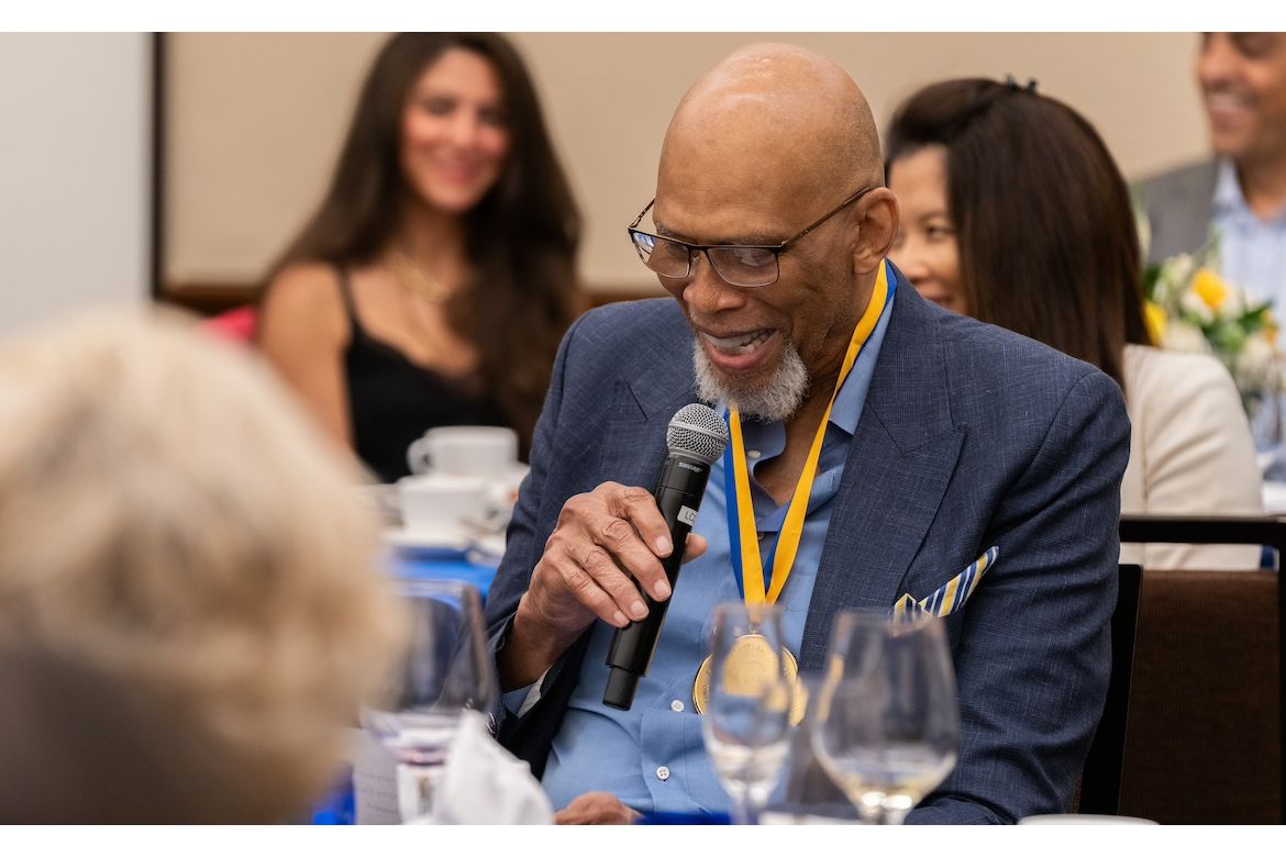 Photo | Abdul-Jabbar talking into microphone at table | UCLA