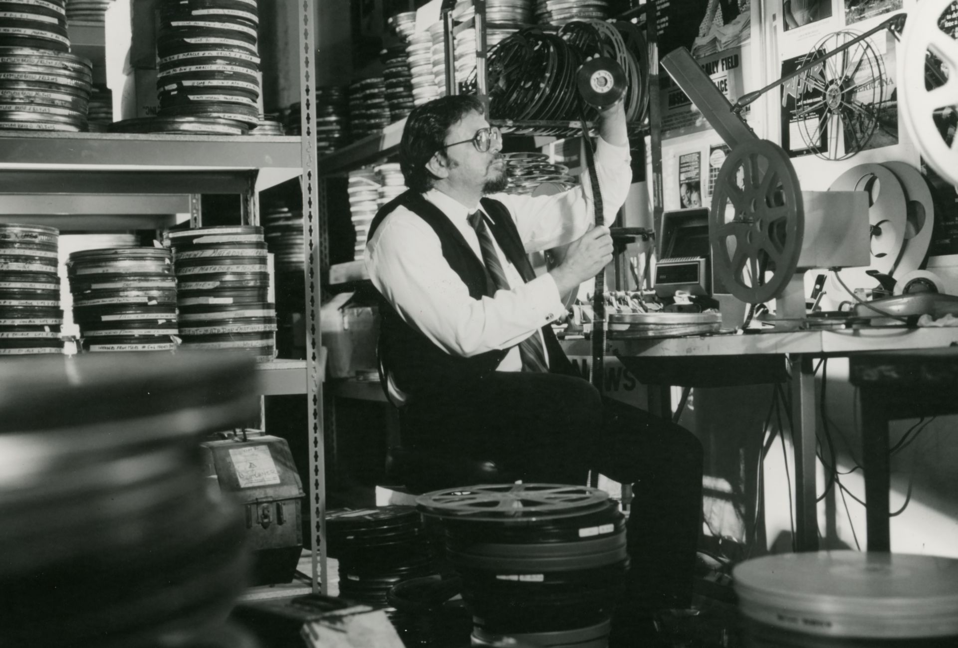 Photo | Robert Rosen sitting at a desk surrounded by film reels | UCLA