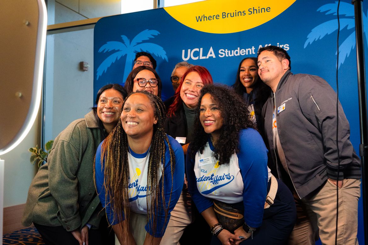 Photo | A group of nine people pose for a shot in front of a blue-and ...