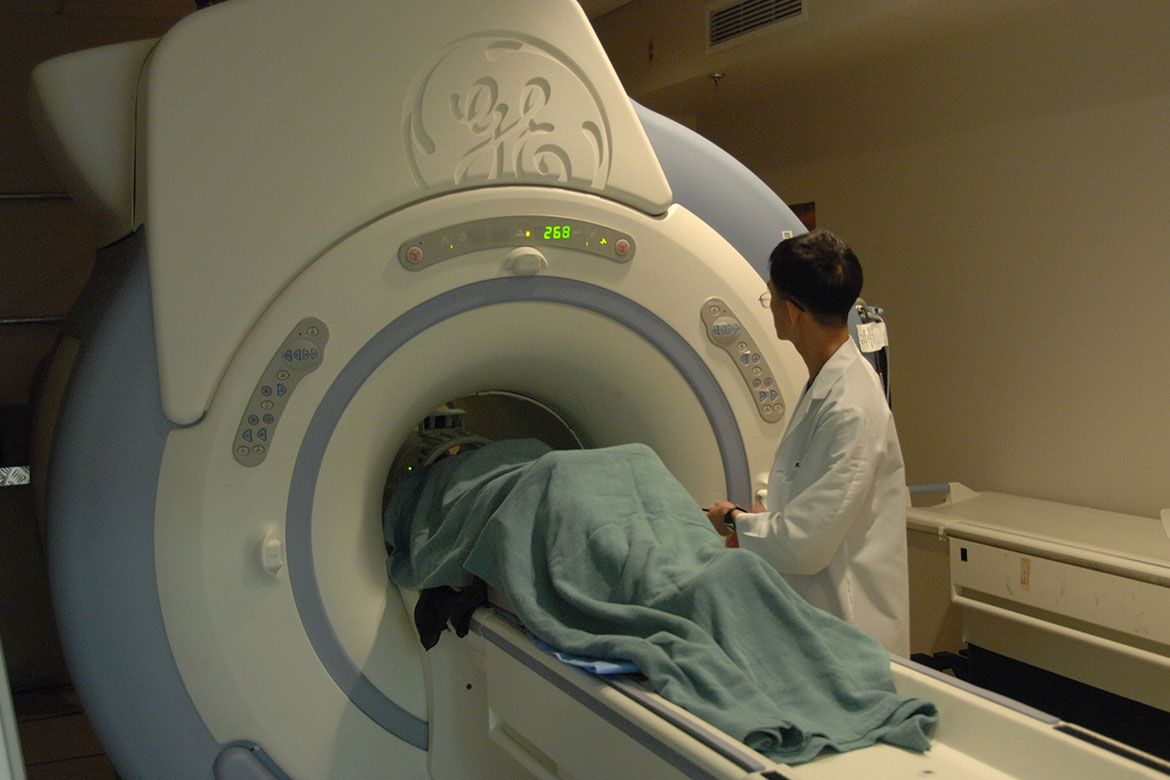 Photo | Technician in white coat stands as a patient undergoes an MRI ...