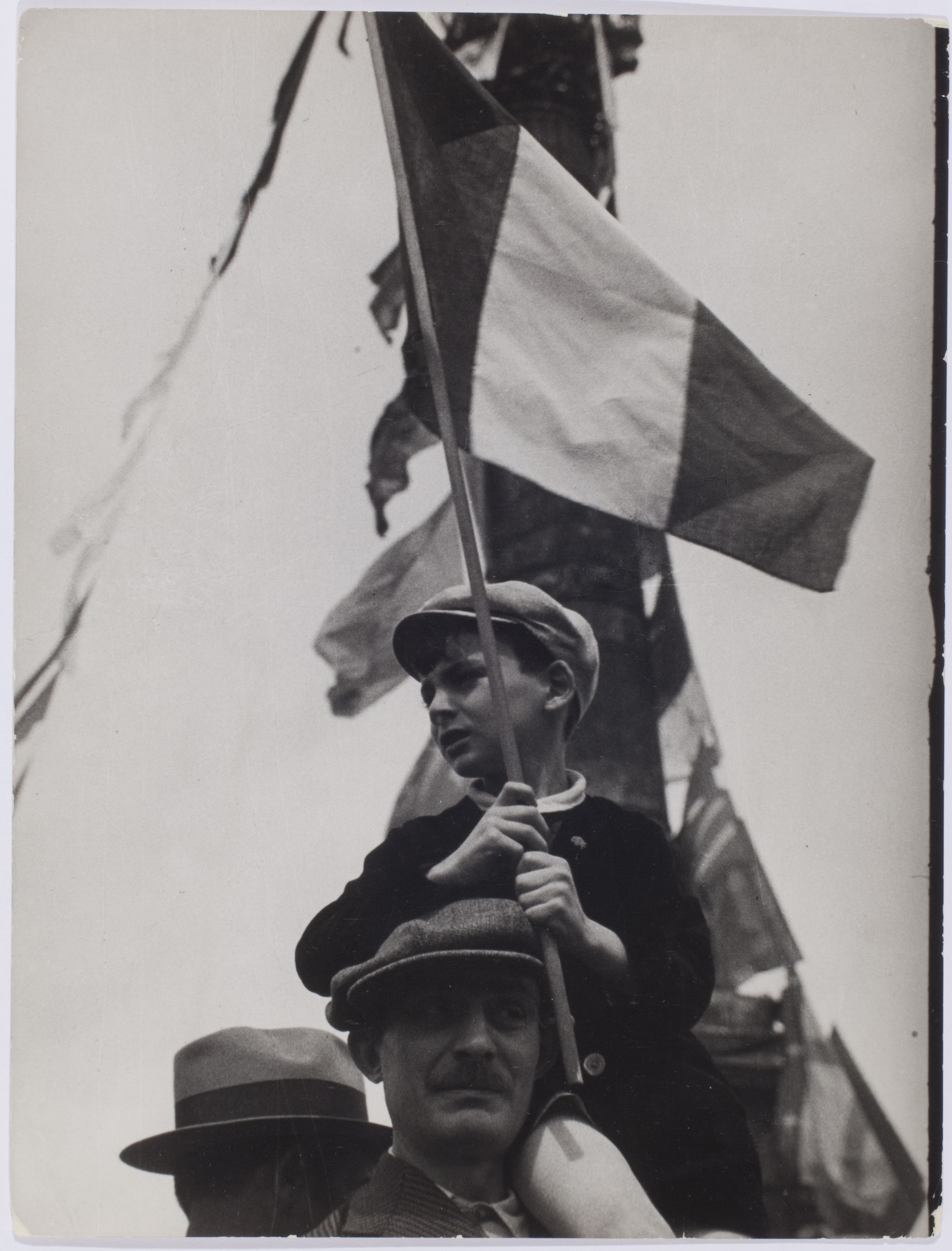 [Boy sitting on man's shoulders holding a French flag on Bastille Day ...