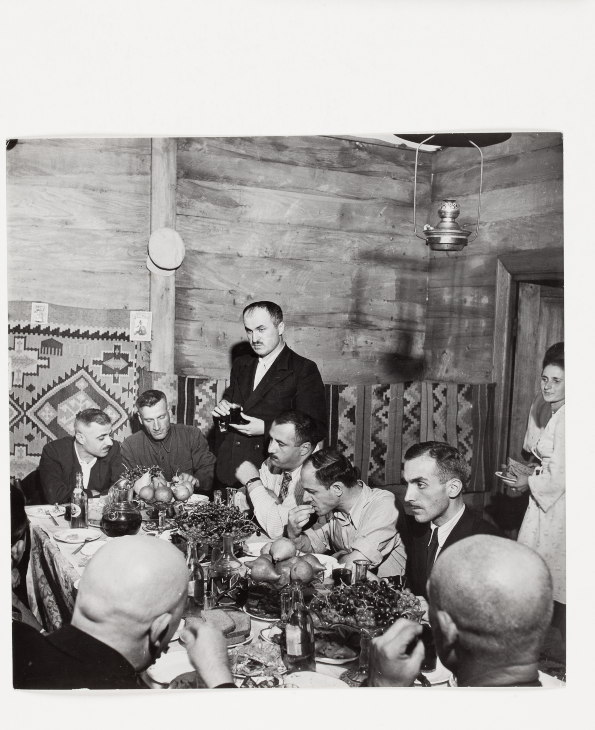 [A man standing with a glass and others eating at the table during a ...