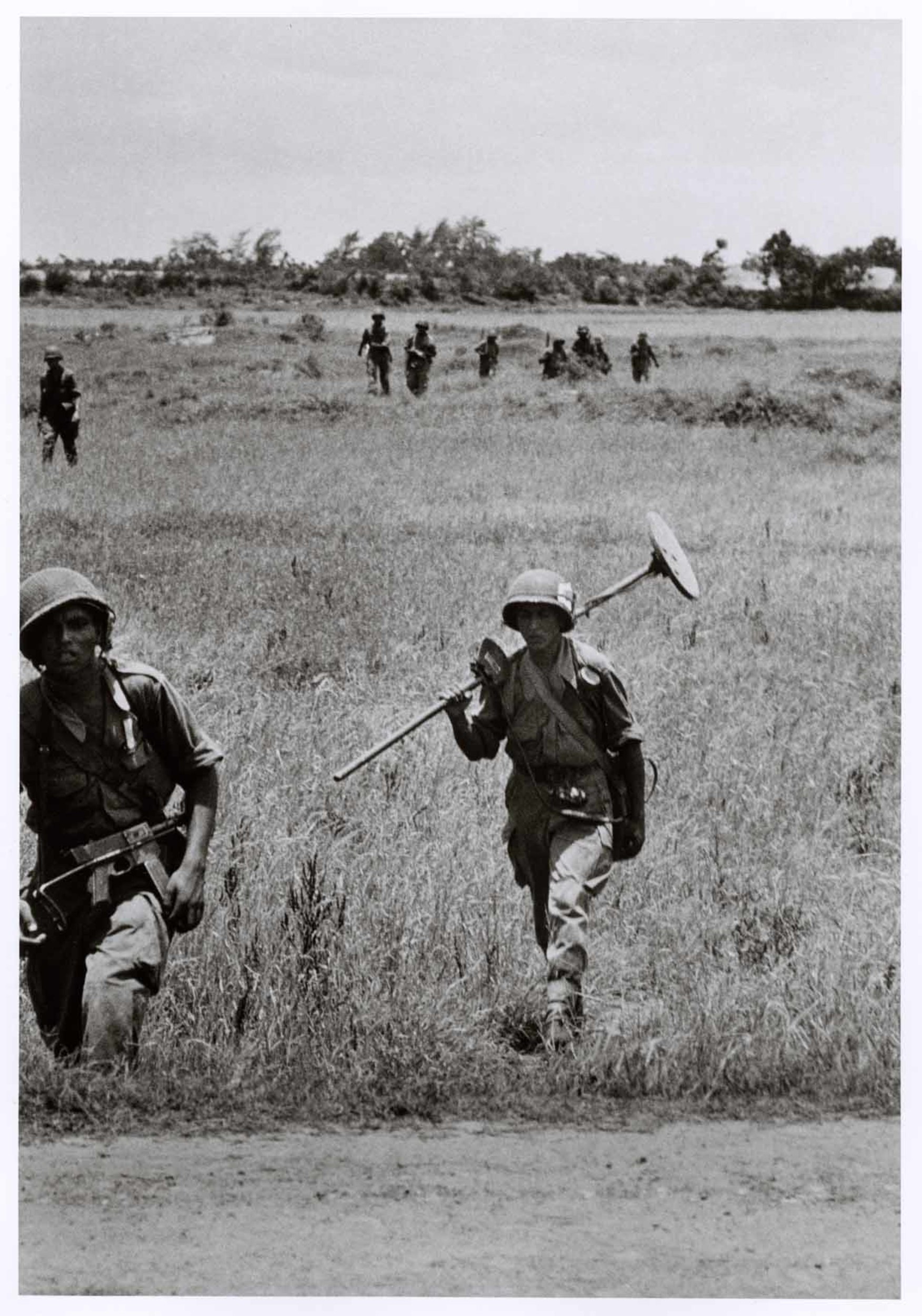 [Men walking out of a field carrying mine detectors over their ...