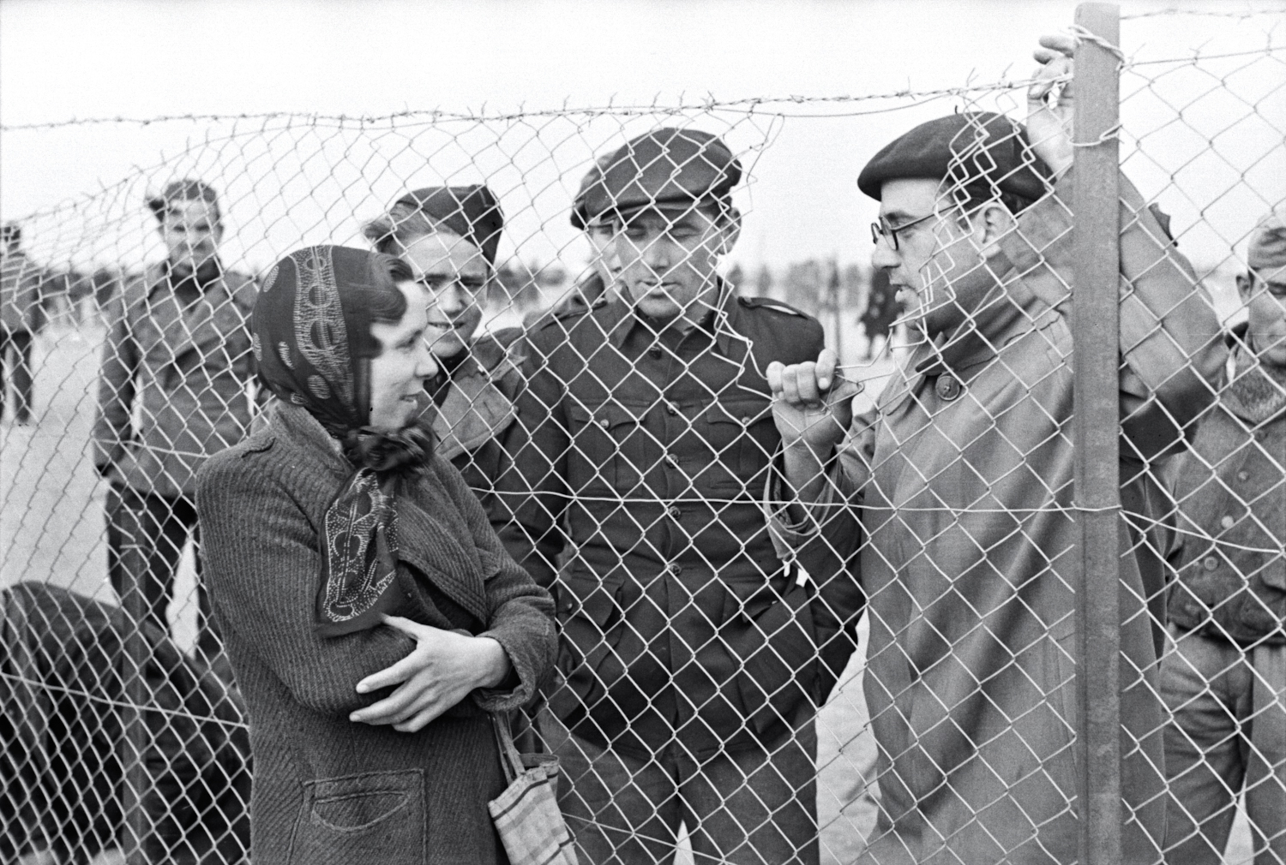 [Men talking to a woman across a fence at an internment camp for ...