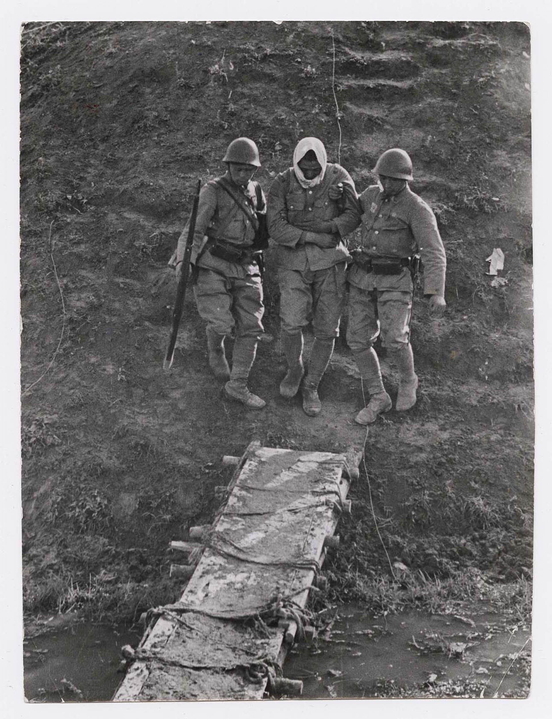 A wounded Japanese is helped by two comrades to an army-made footbridge ...