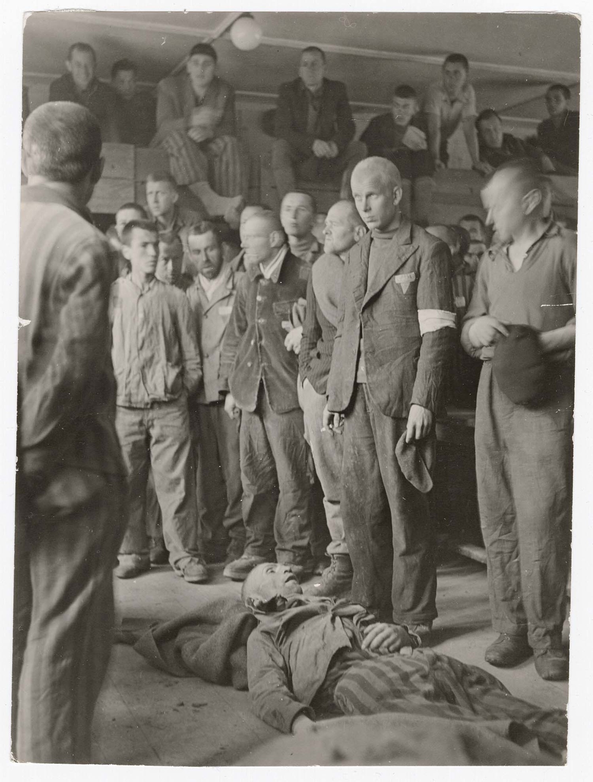 Dachau prisoners solemnly standing around a fellow prisoner as he dies ...