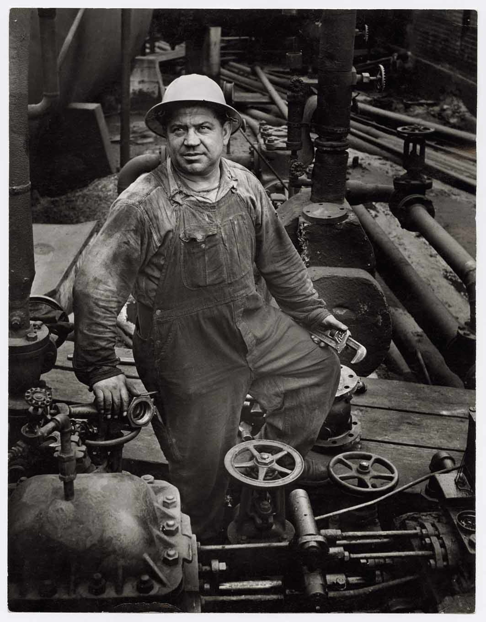 [Helmeted worker in overalls holding wrench by valves] | International ...