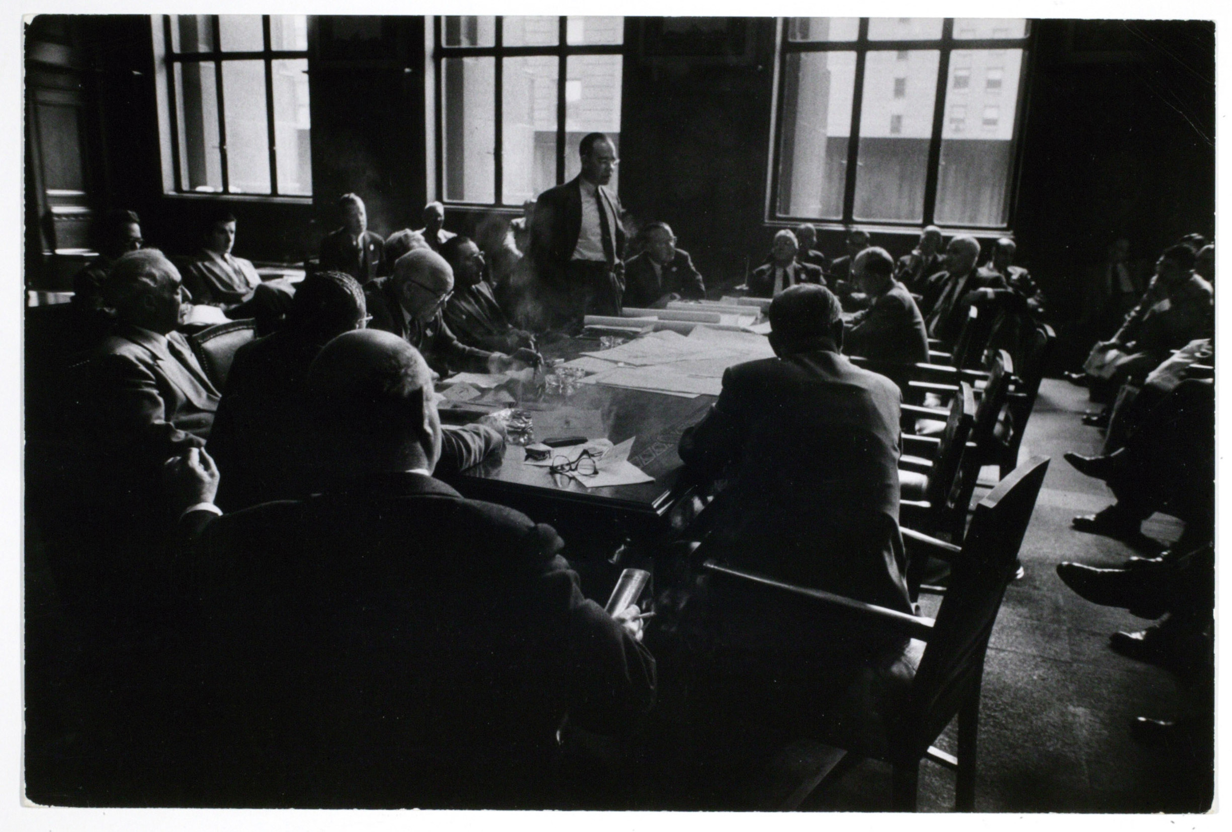 [Men seated and one man standing around conference table with ...
