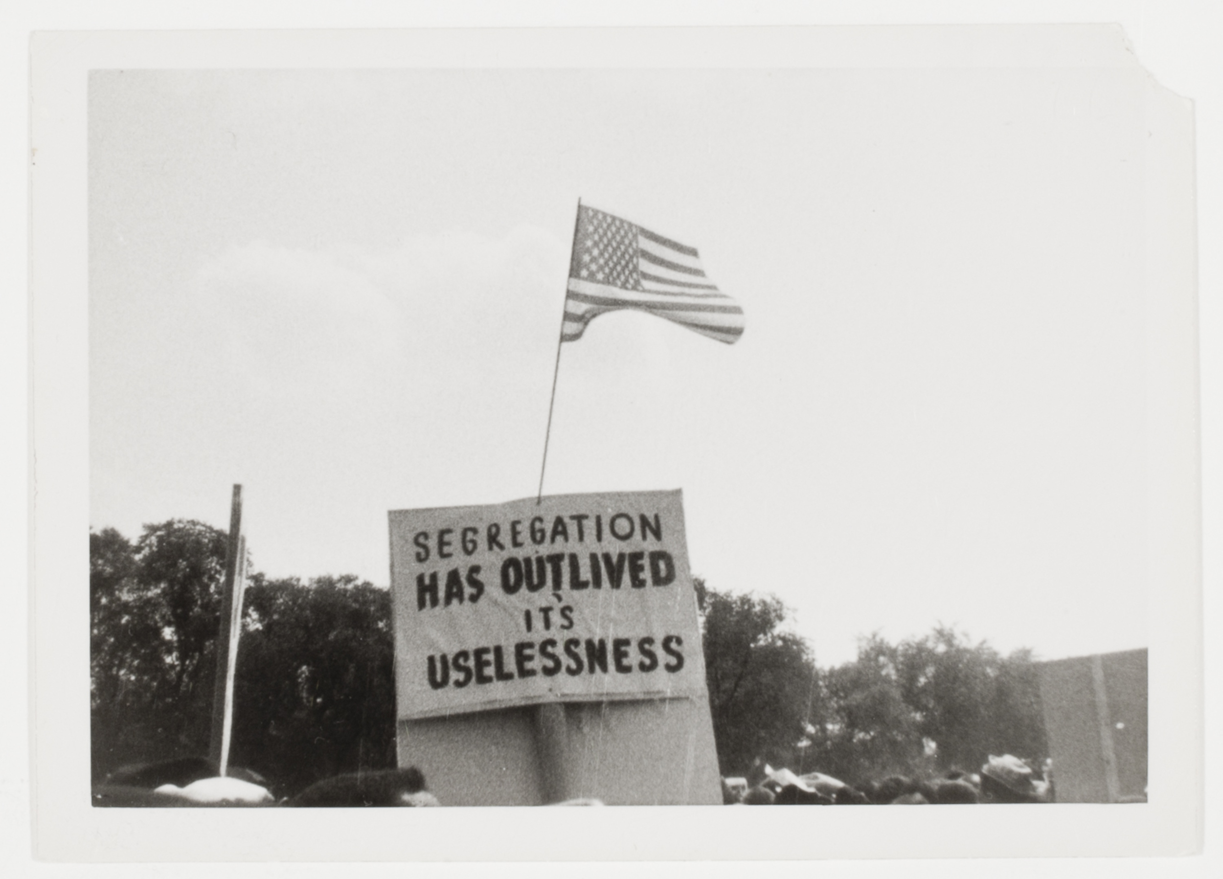 [American flag waving above a sign that reads "Segregation has outlived ...