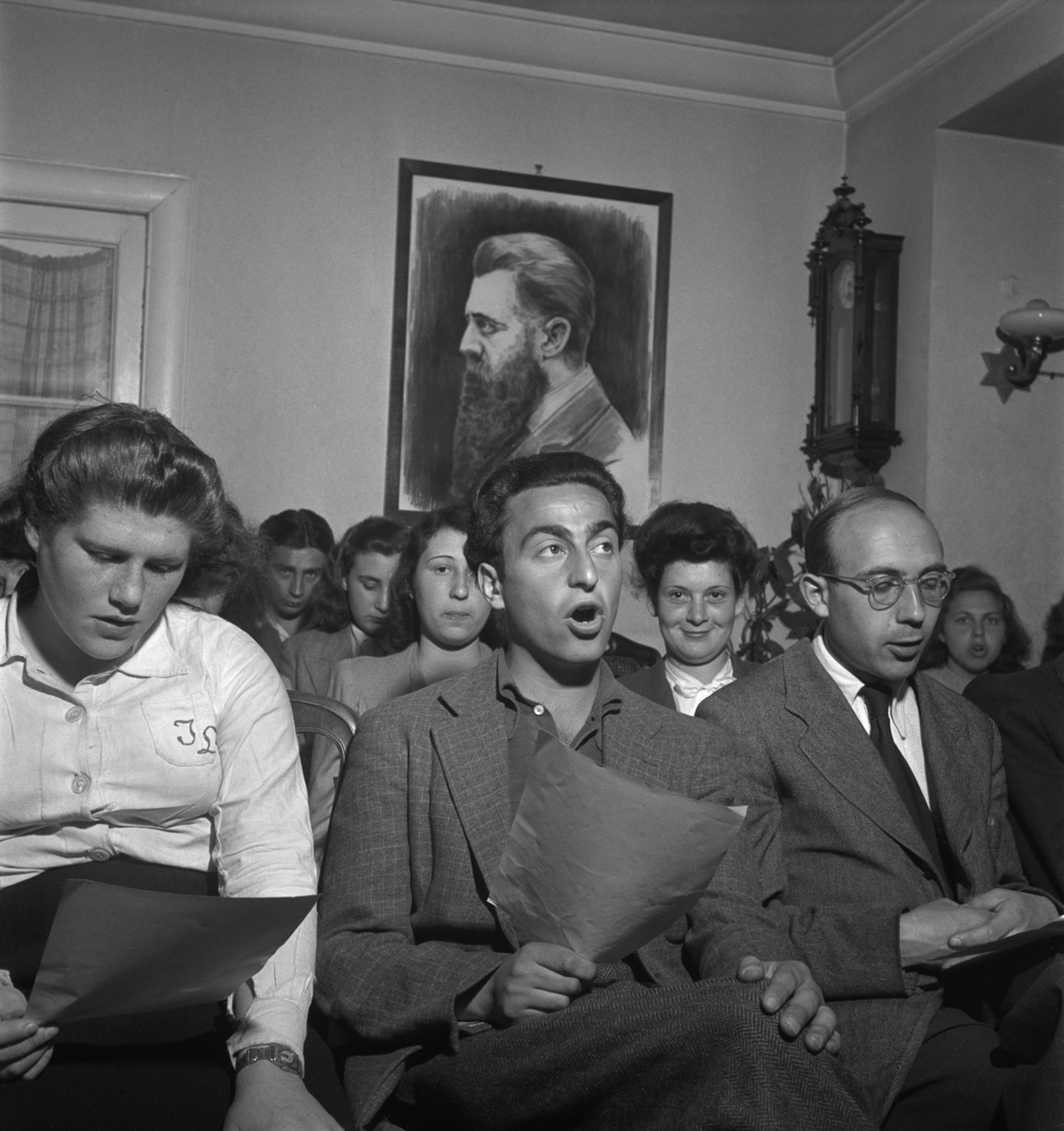 [Jewish refugees singing in front of a portrait of Theodor Herzl ...