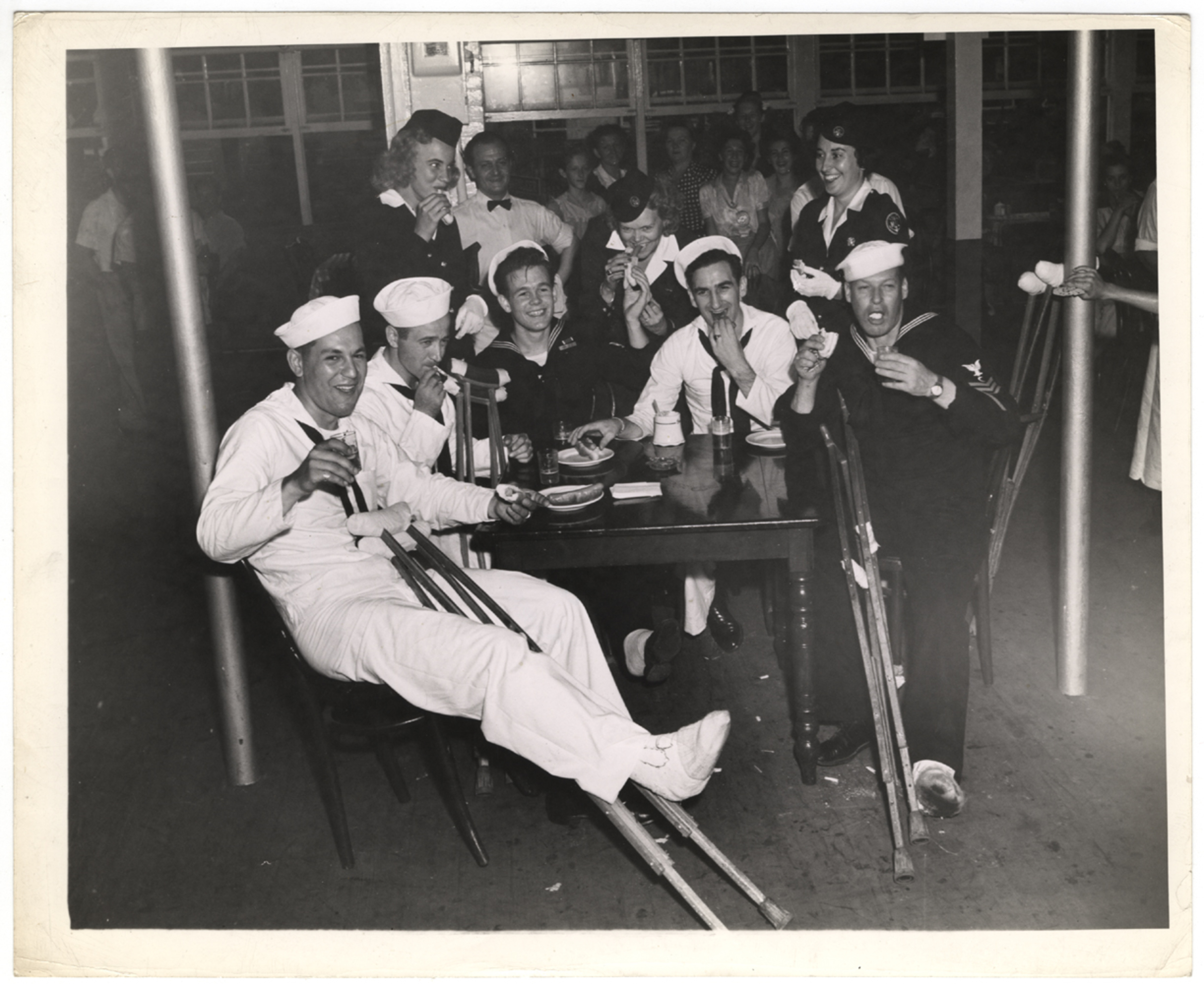[Sailors, some injured with crutches, eating hot dogs and laughing ...