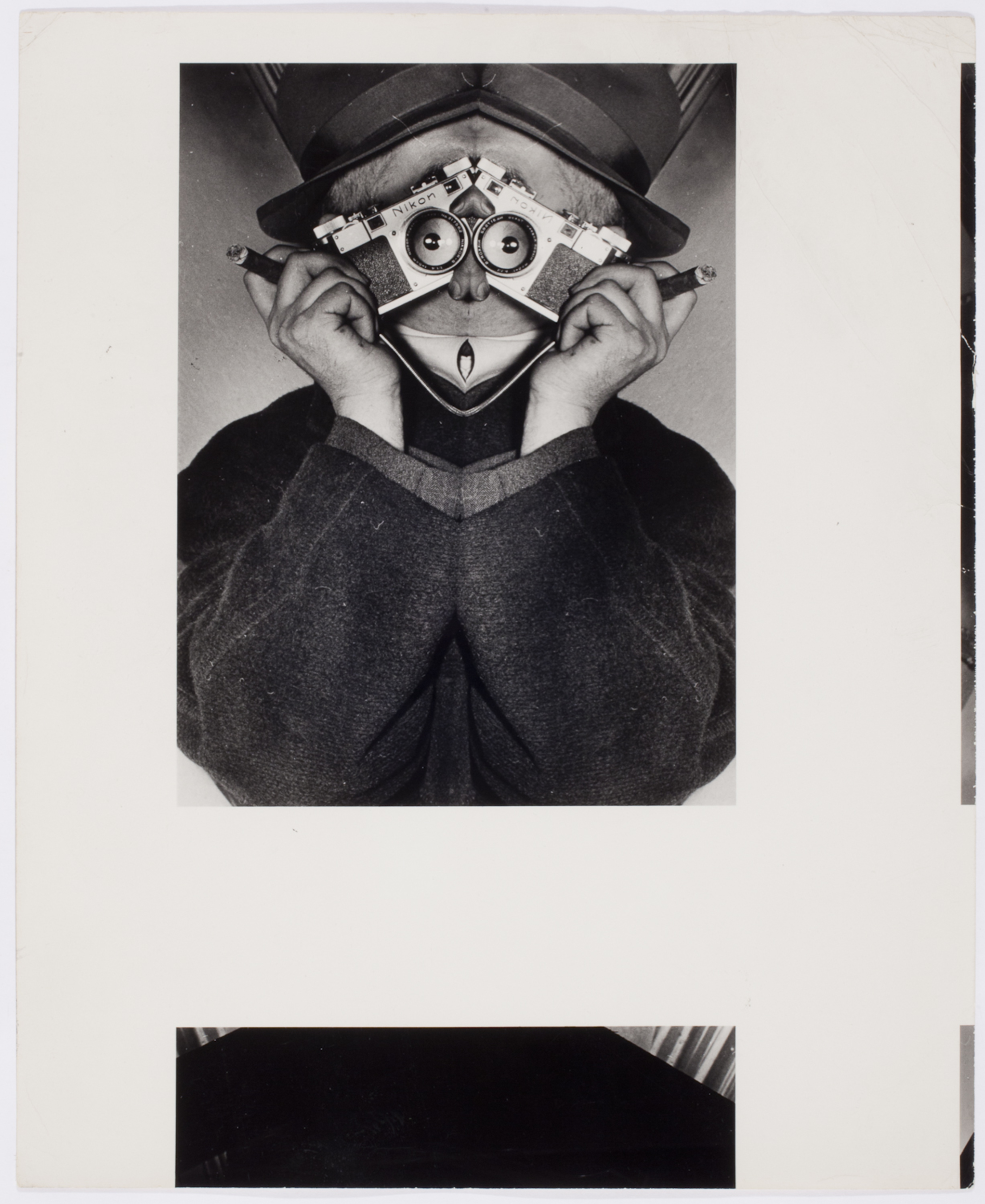 [Weegee self-portrait holding a 35 mm camera and a cigar, wearing a hat ...