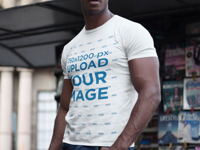 Placeit - T-Shirt Mockup Featuring a Man Posing Near a Newspaper Stand